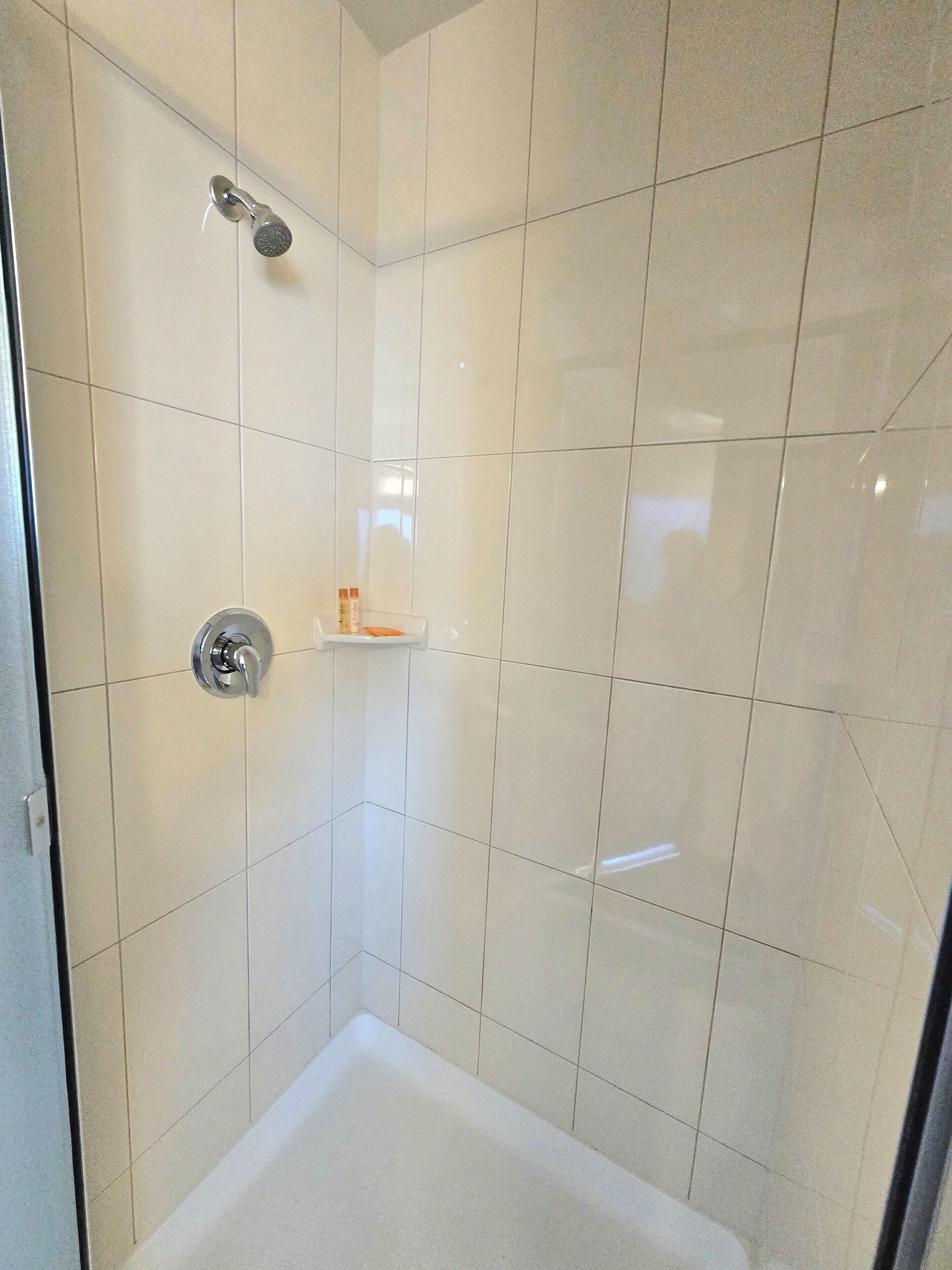 Pequena área de chuveiro com azulejos, chuveiro manual e torneira fixada na parede.