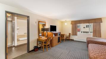 Quarto de hotel com cama, escrivaninha com cadeira, televisão e banheiro visível por uma porta aberta.
