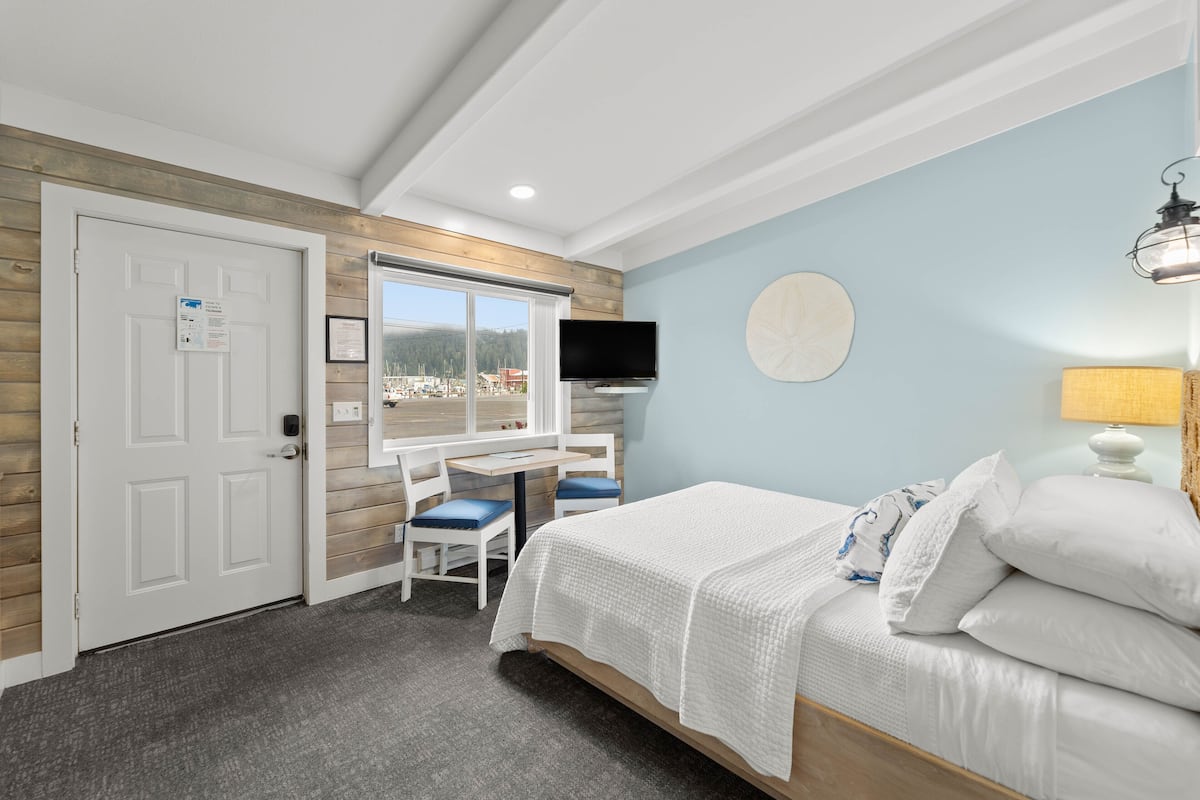 Quarto com cama, escrivaninha e cadeira, TV na parede e janela com vista para a praia.