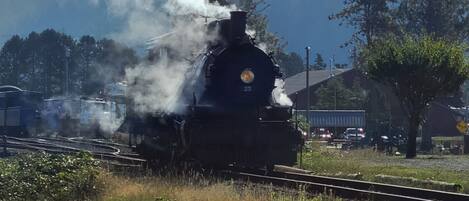 Uma locomotiva a vapor com fumaça saindo da chaminé, percorrendo um trilho de ferro.