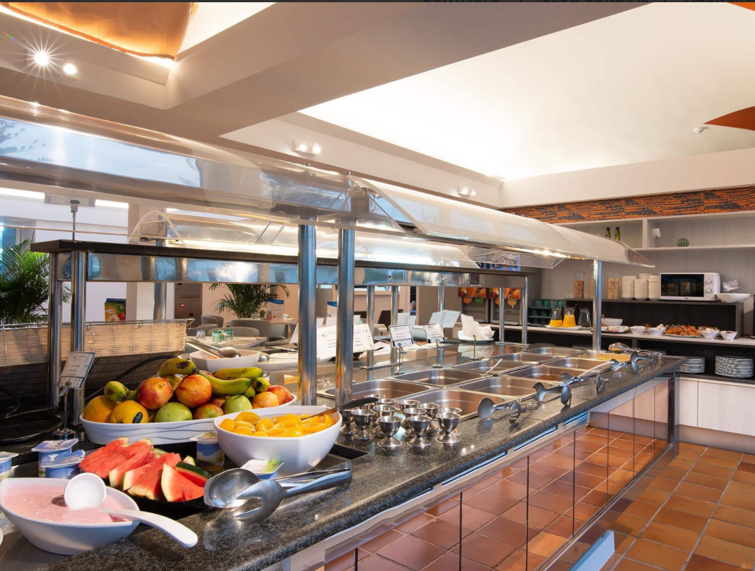 Disposição moderna de buffet com diversas frutas, potes de iogurte e utensílios.