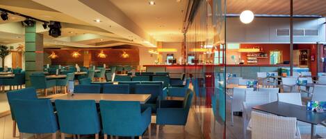 Um restaurante espaçoso com mesas e cadeiras altas, um bar e uma área de estar com cadeiras estofadas.