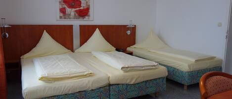 Quarto de hotel com duas camas, cada uma com cabeceira de madeira e colcha estampada. Há um quadro na parede acima das camas.