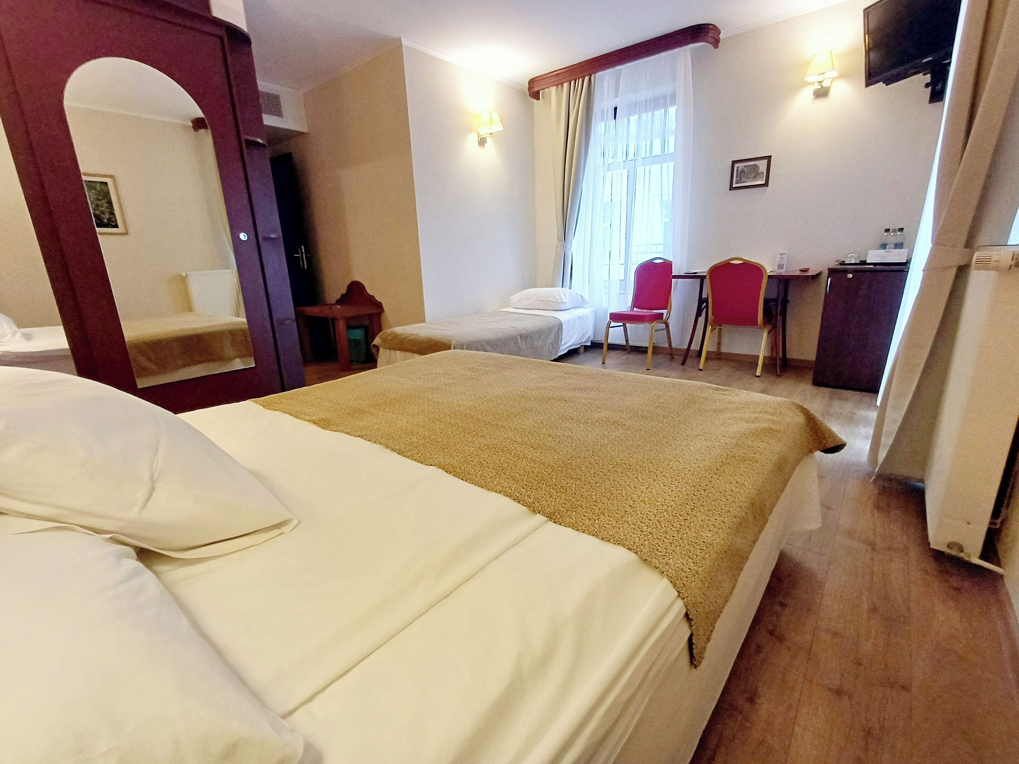 Quarto de hotel com cama, escrivaninha, cadeira, televisão e espelho.