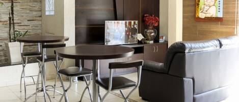 Um hall de hotel moderno com um sofá, duas mesas redondas e quatro banquetas de bar.