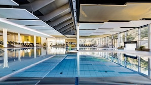 Piscina interior moderna com água cristalina, um dreno central e uma área ensolarada com assentos.