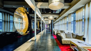 Um lobby moderno de hotel com um corredor longo, área de estar e janelas amplas.