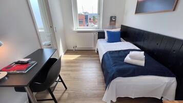 Quarto de hotel com cama, escrivaninha, cadeira, janela e um quadro na parede.