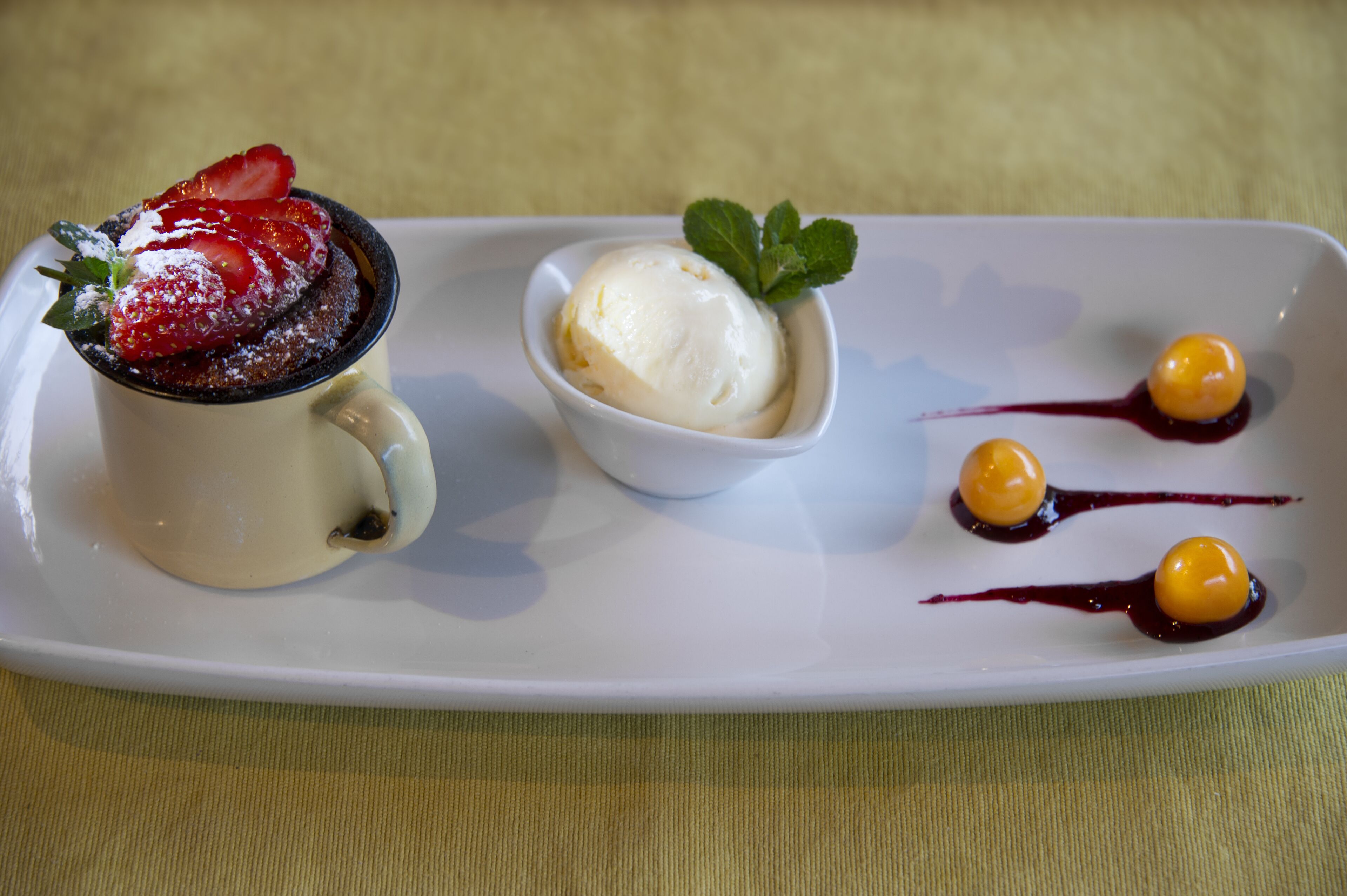 Um prato de sobremesa com um doce de chocolate, uma bola de sorvete de baunilha e duas porções de molho.