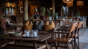Interior acolhedor e rústico com móveis de madeira, parede de pedra e luminárias de vime penduradas.