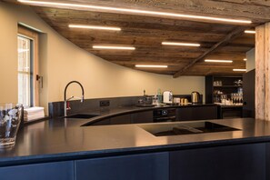 Cozinha moderna com bancada curva, eletrodomésticos embutidos e teto de madeira com vigas aparentes.