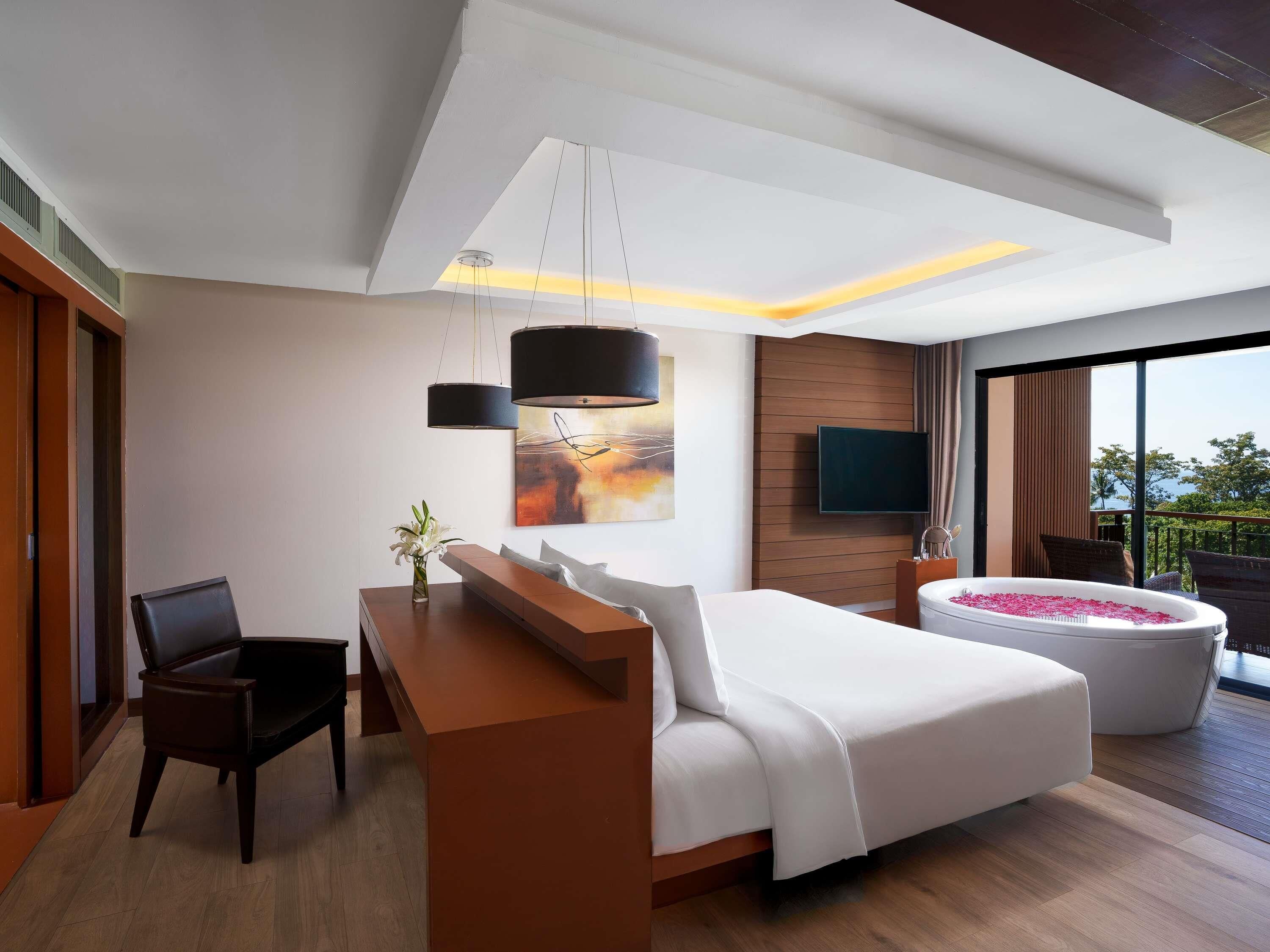 Quarto de hotel moderno com uma cama grande, uma escrivaninha, uma cadeira, uma televisão e varanda com hidromassagem.