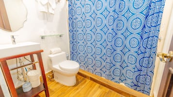 Um banheiro com pia branca, vaso sanitário, penteadeira de madeira e cortina de chuveiro estampada em azul.