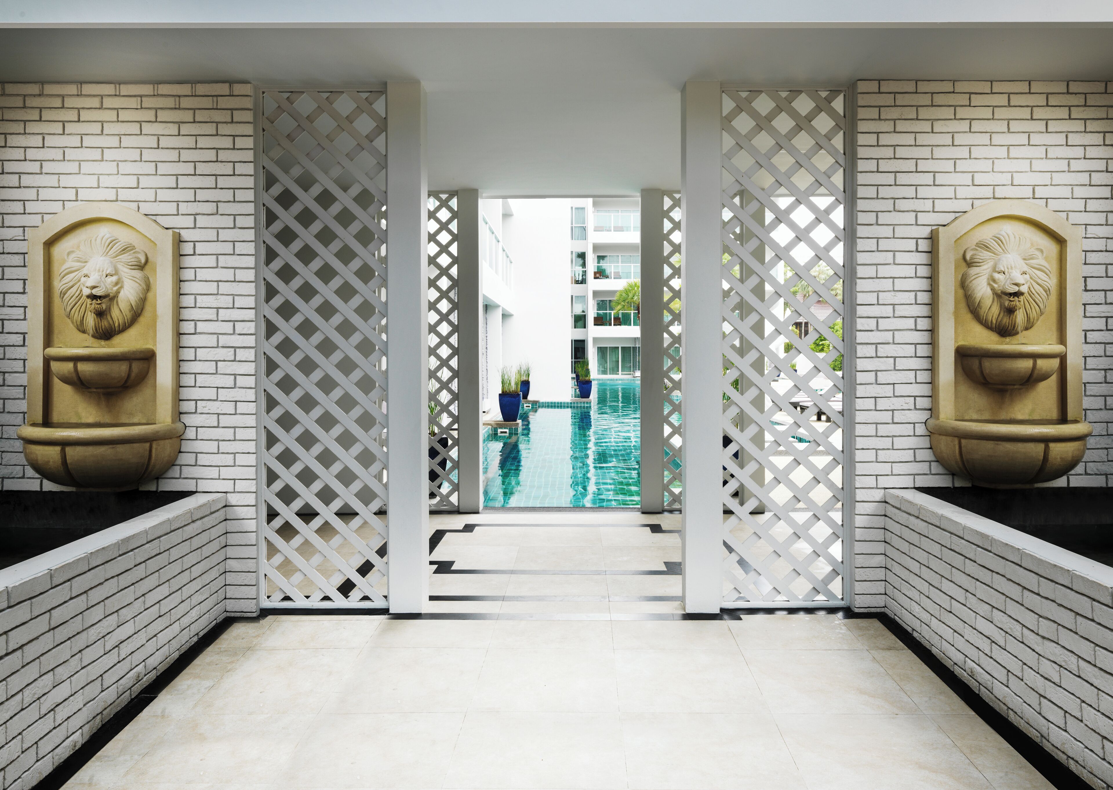 Um saguão de hotel moderno com vista para a piscina, paredes de tijolo branco e esculturas decorativas de cabeças de leão.