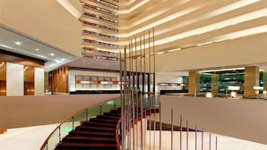 Interior moderno de hotel com escadaria espiral central, vários andares e elementos de design contemporâneos.