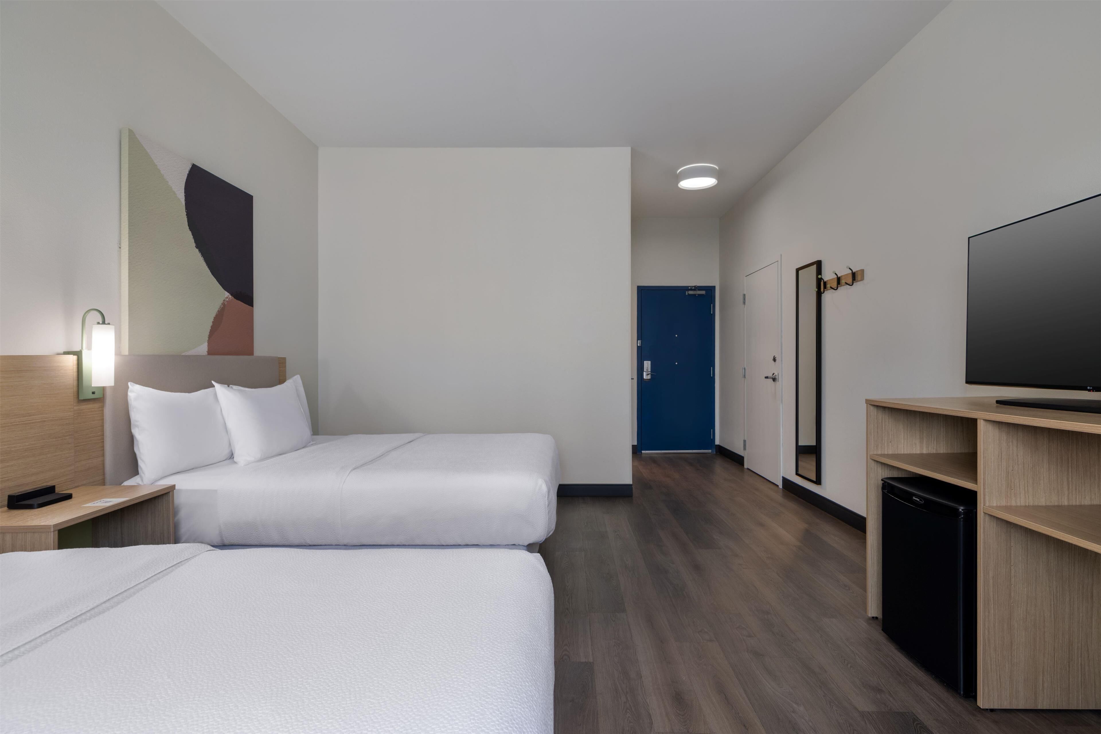 Quarto de hotel com duas camas, uma escrivaninha, uma televisão e um pequeno frigorífico.