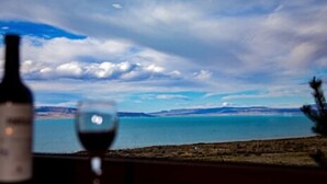 Uma garrafa de vinho e um copo sobre uma mesa, com vista para a água e montanhas ao longe.