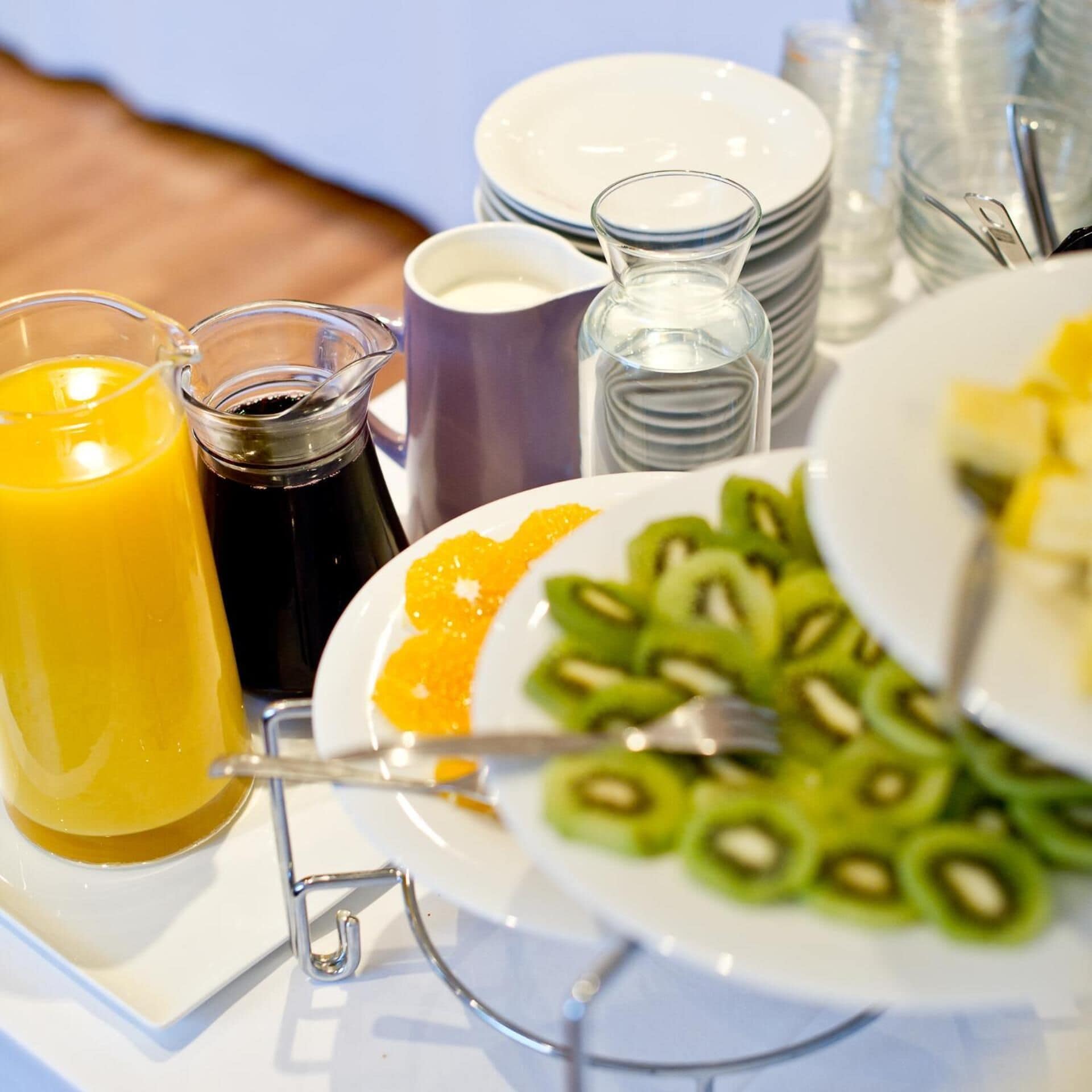 Uma mesa de café da manhã com uma fatia de kiwi, um copo de suco de laranja e um copo de café preto.