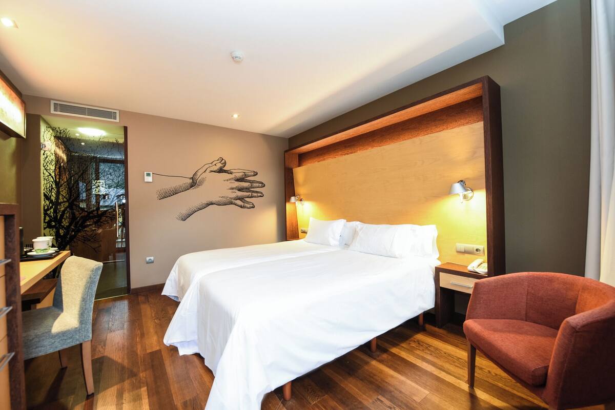 Quarto de hotel com cama, escrivaninha, cadeira e uma obra de arte na parede.