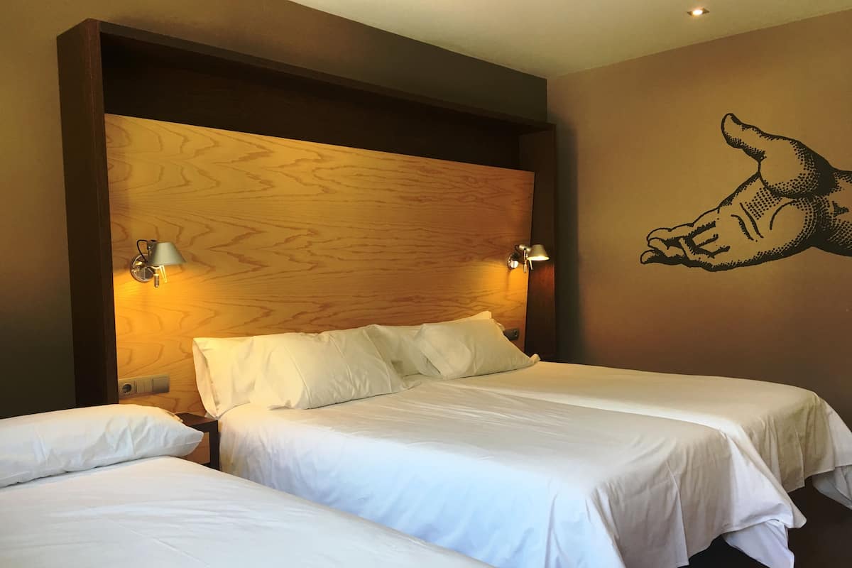 Quarto de hotel com duas camas, cabeceira de madeira, luminárias fixadas na parede e um mural de uma mão.