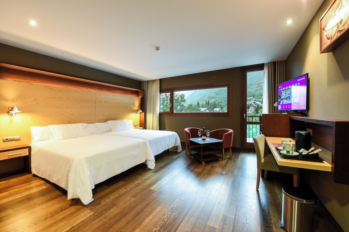 Quarto de hotel com duas camas, uma escrivaninha com cadeira, televisão e vista para o exterior.
