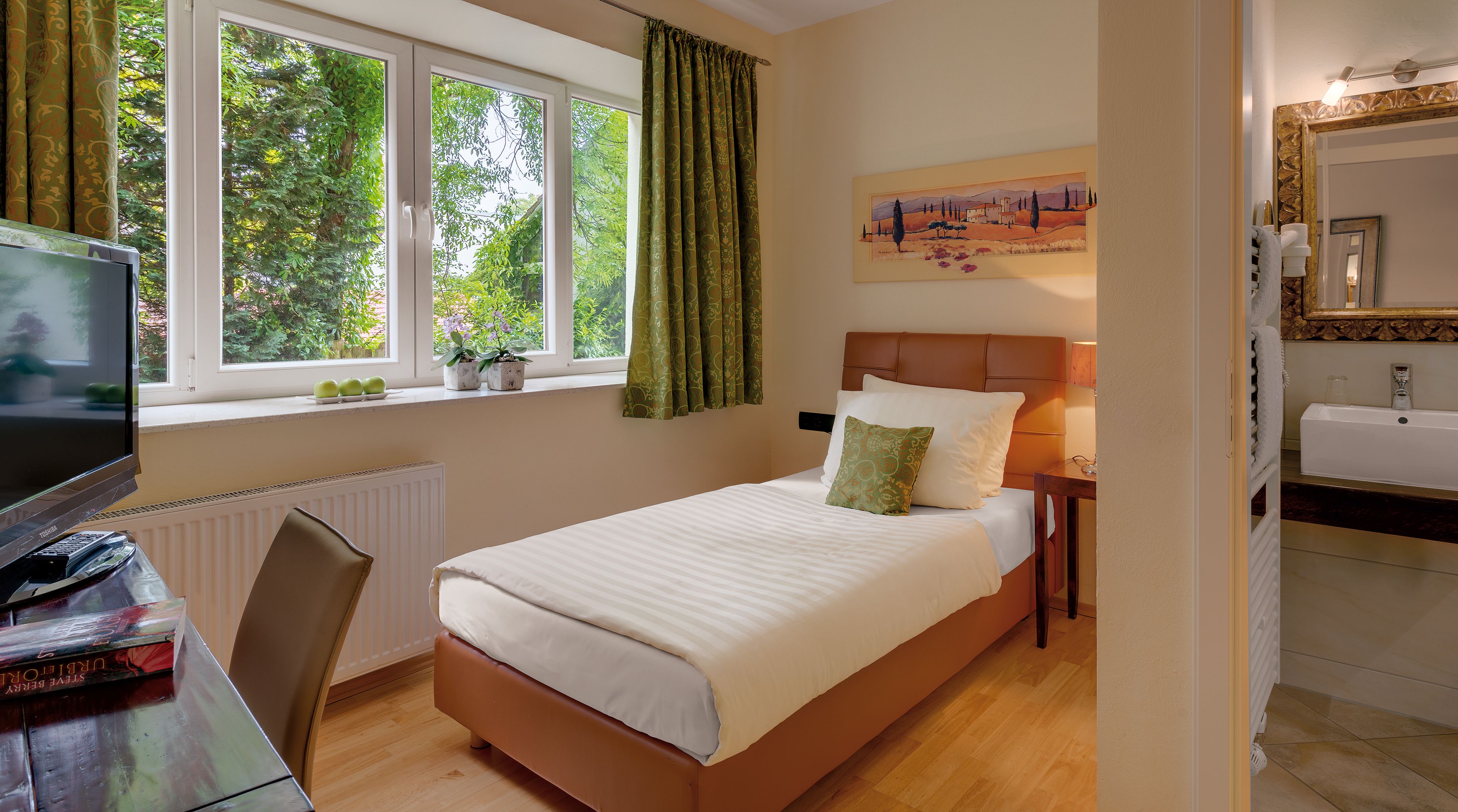 Quarto de hotel com cama, televisão, escrivaninha e janela com cortinas.