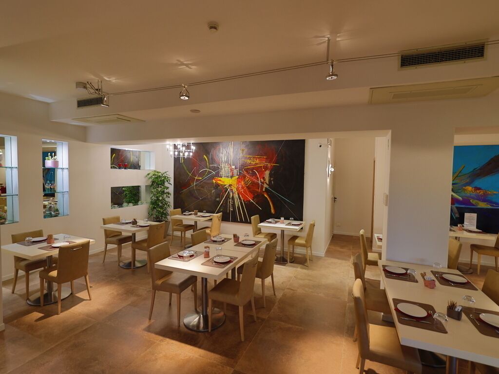 Uma sala de jantar com várias mesas e cadeiras, um grande quadro abstrato na parede e uma planta no canto.