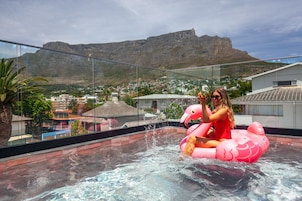 Piscina com barreira de vidro, boia de flamingo rosa e vista para uma cidade com edifícios e montanha ao fundo.