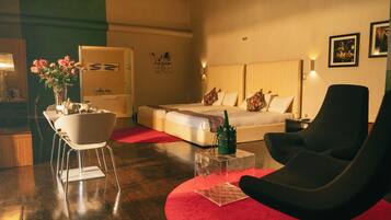Quarto de hotel moderno com teto de madeira, cama com várias almofadas, poltrona preta, mesa de jantar com cadeiras e tapete vermelho.