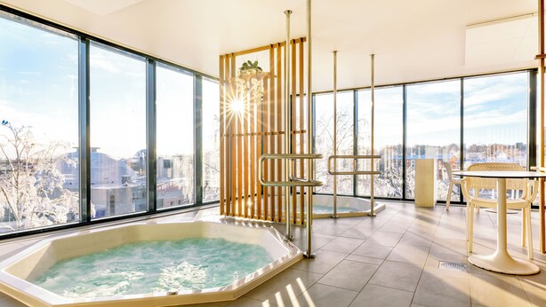 Um spa moderno com uma banheira de hidromassagem grande, janelas amplas e vista para a cidade.