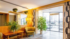 Um saguão de hotel moderno com um balcão de recepção de madeira, uma poltrona confortável e amplas janelas com vista para a cidade.