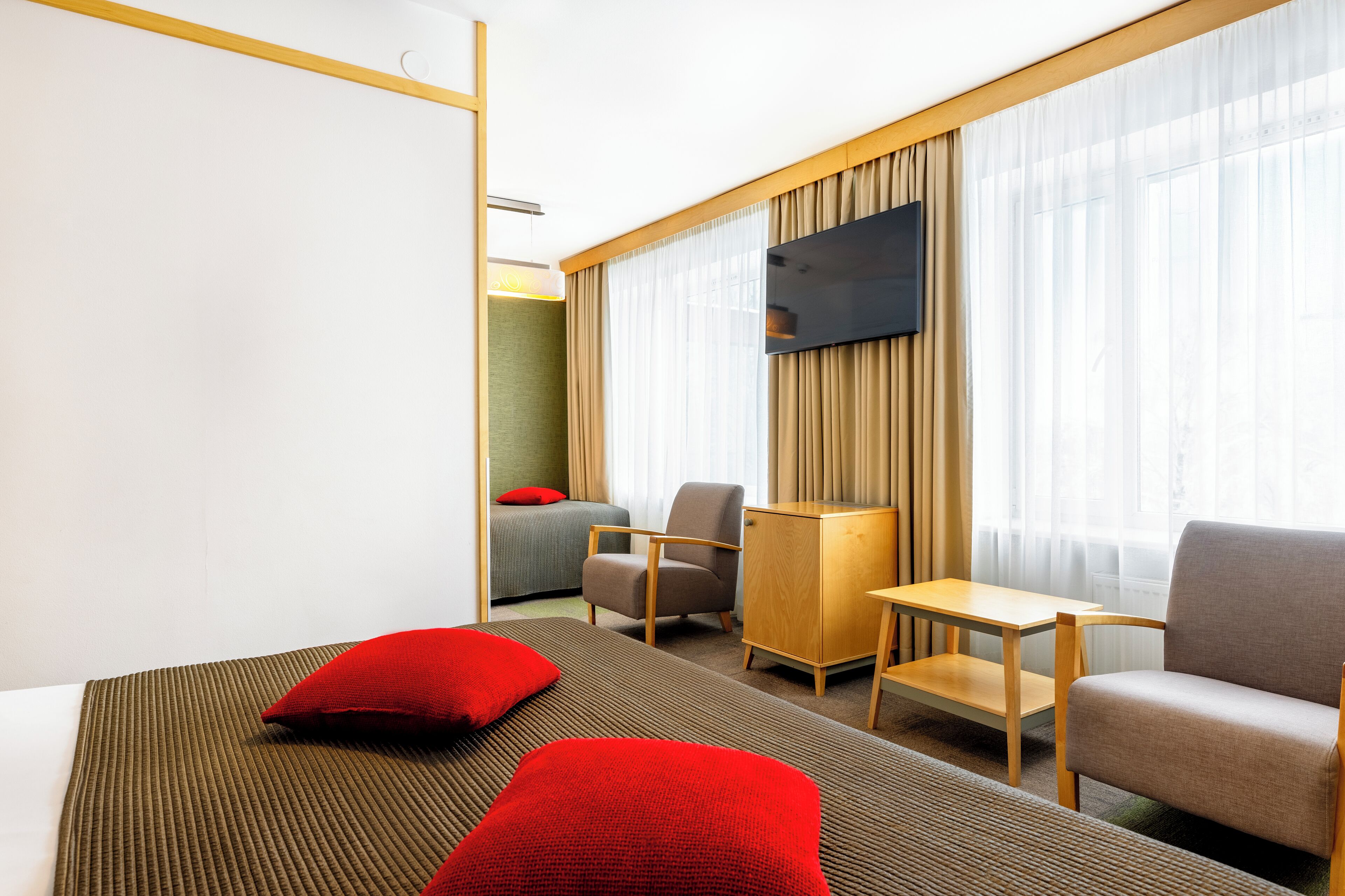 Quarto de hotel com cama, escrivaninha, cadeira, televisão e janela com cortinas.