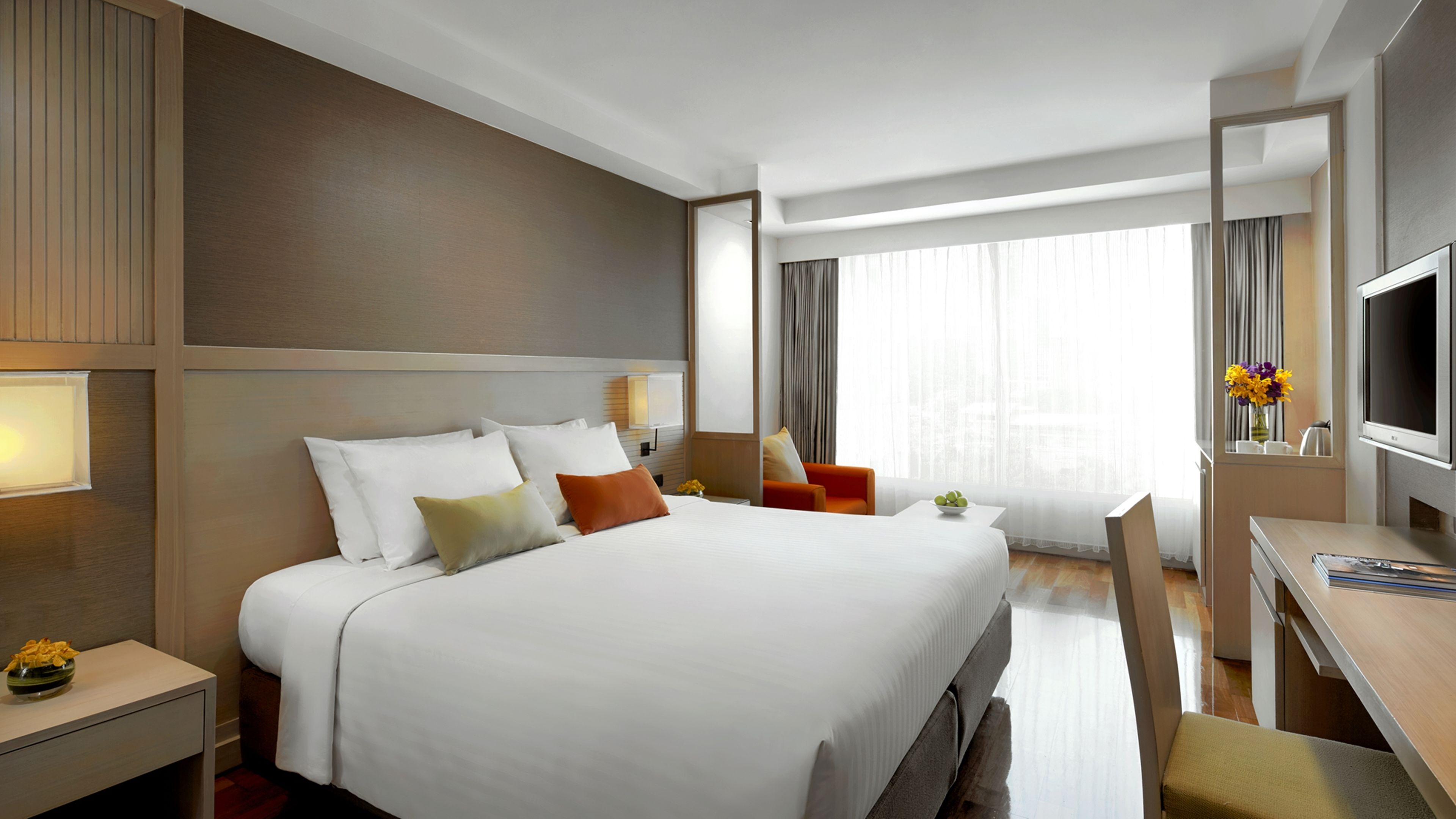 Quarto de hotel com uma cama grande, uma escrivaninha, uma cadeira, uma televisão e uma janela com cortinas.