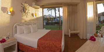 Quarto de hotel com cama, mesa de cabeceira, escrivaninha e uma cadeira, e vista para o exterior.