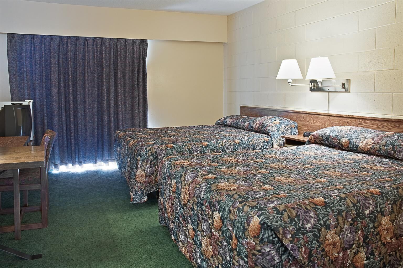Quarto de hotel com duas camas, uma escrivaninha e uma cadeira.