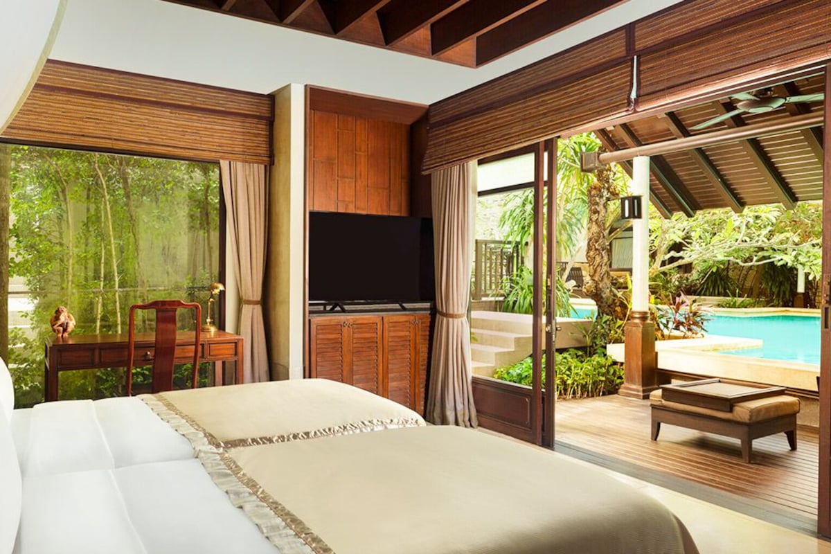 Quarto com cama, televisão, escrivaninha e vista para uma piscina.