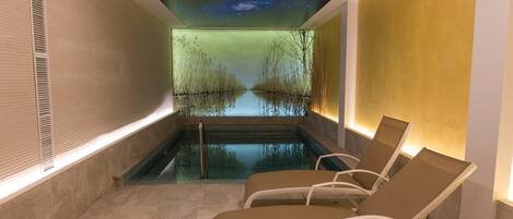 Uma área de piscina interior moderna com teto estrelado, espreguiçadeiras e um elemento aquático relaxante.