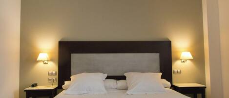 Quarto de hotel com uma cama grande, duas mesas de cabeceira e luminárias de parede.