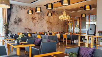 Um restaurante moderno com mesas e cadeiras altas, um grande candelabro e uma parede rústica.