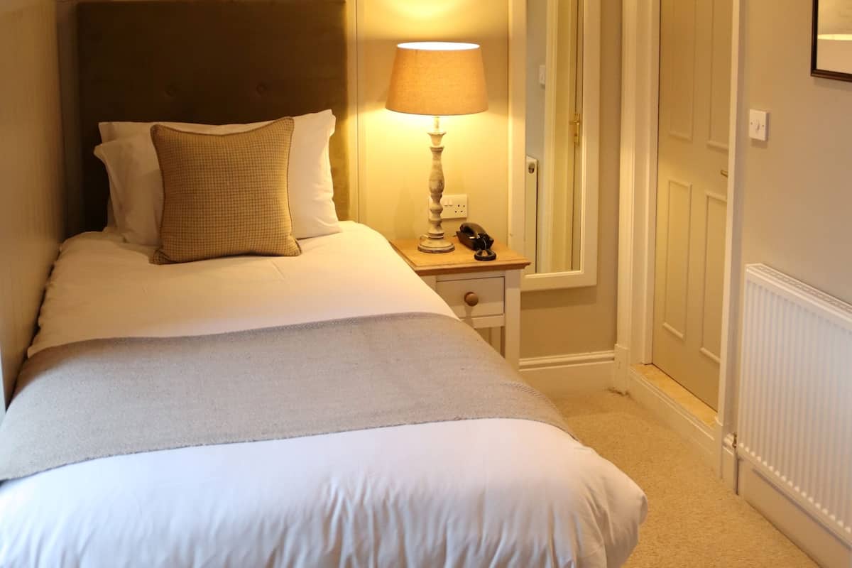 Um quarto com uma cama, uma mesa de cabeceira, um abajur, uma porta e um radiador.