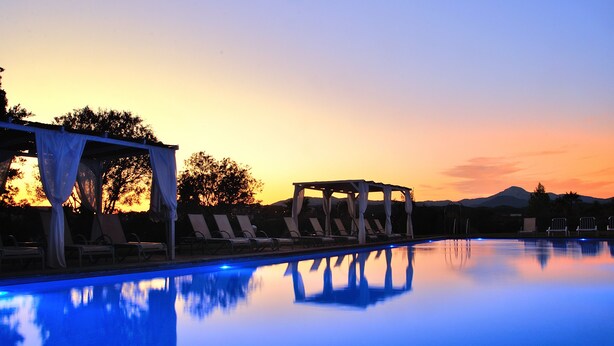 Uma piscina com espreguiçadeiras e um gazebo ao pôr do sol.