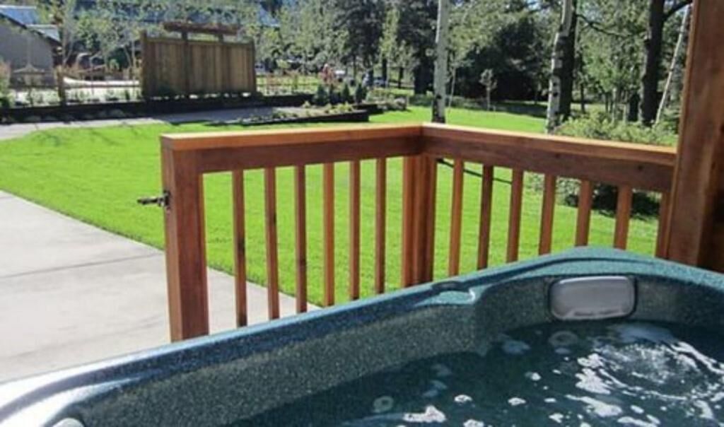 Uma banheira de hidromassagem com um deck de madeira e vista para um gramado bem cuidado e árvores.