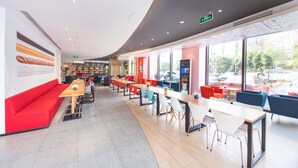 Um café moderno com várias áreas de estar, incluindo sofás vermelhos e mesas com cadeiras.