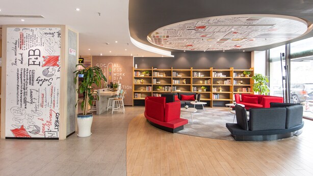 Uma biblioteca moderna com assentos vermelhos e pretos, estantes de madeira e um grande elemento circular no teto.