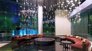 Um lobby moderno com um sofá vermelho curvo, um banquinho preto redondo e luminárias pendentes.