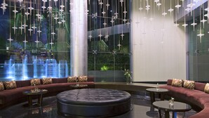 Um lobby moderno com área de estar, luminárias pendentes e vista para uma cascata.