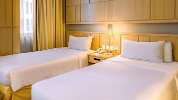 Quarto de hotel com duas camas, uma mesa de cabeceira com abajur e cabeceira de madeira.
