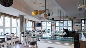 Uma área de bar moderna com balcão de vidro, vários bancos e luminárias esféricas penduradas.