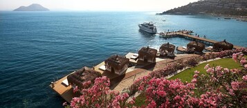 Um resort costeiro com cabanas de telhado de palha, um píer e um barco atracado ao fundo.
