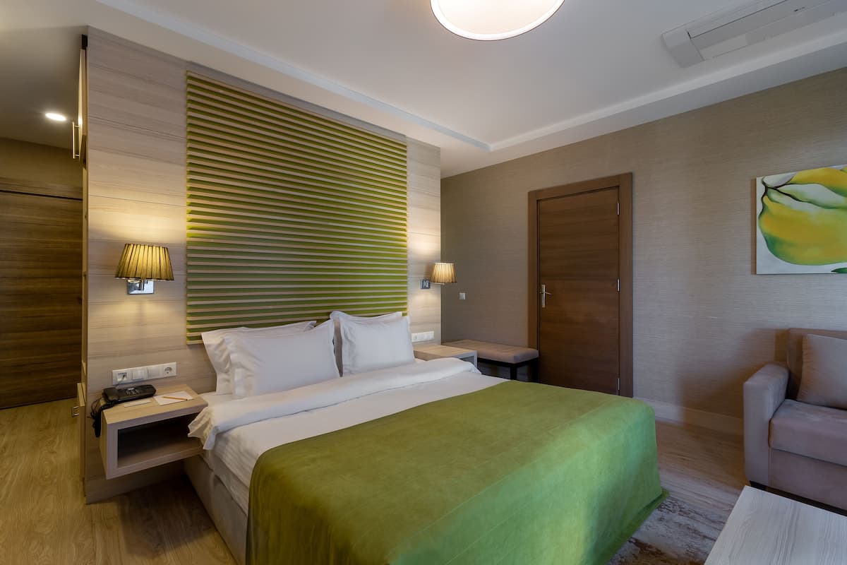Quarto de hotel moderno com cama, mesas de cabeceira, luminária, guarda-roupa de madeira e um quadro na parede.